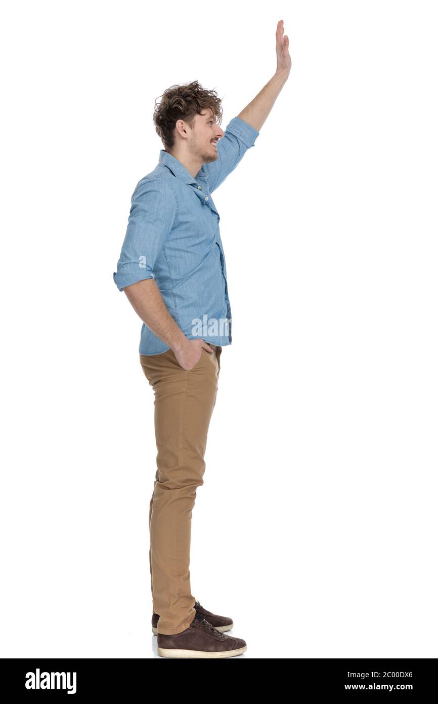 side view of happy young casual guy holding hand up and saluting ...