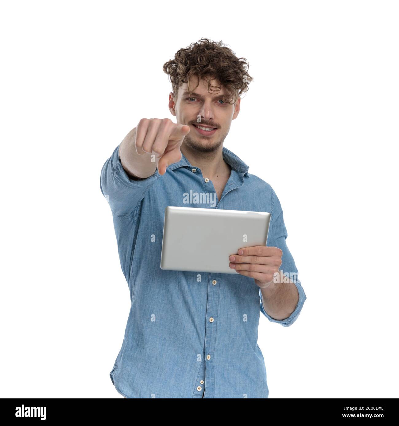 young casual guy smiling, holding tab and pointing finger, standing ...