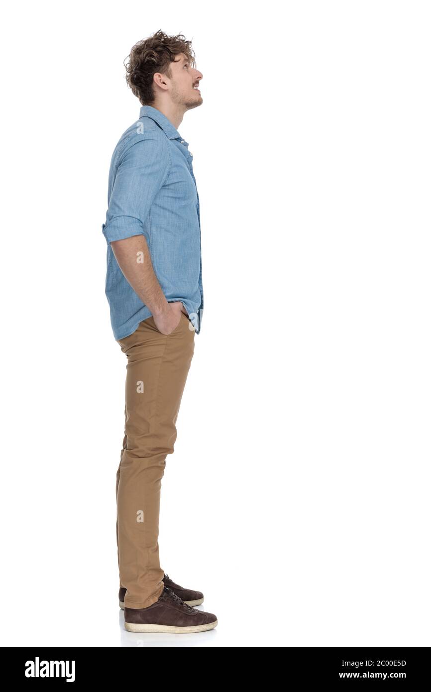 side view of casual model holding hands in pockets and looking up ...