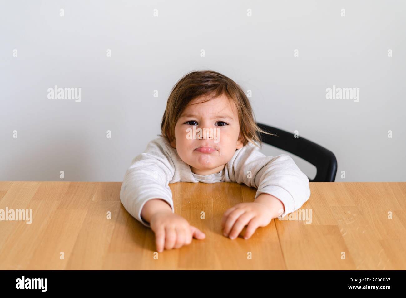 Toddler girl unhappy sitting at wooden desk. Tired child, hungry kid ...