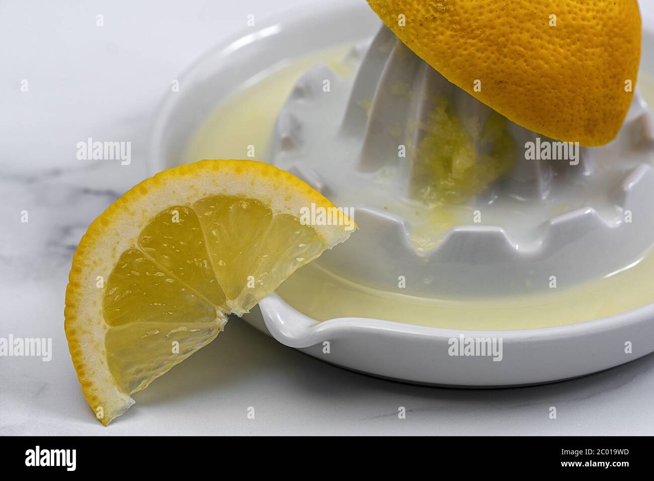 half a lemon squeezed with a porcelain citrus press with a lemon wedge ...