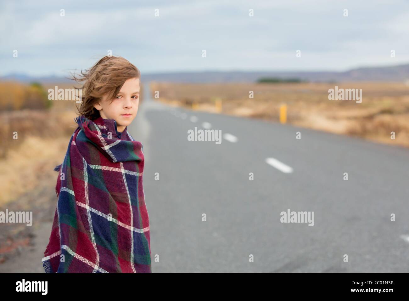 Beautiful child, standing on a road on a very windy day, wrapped in ...