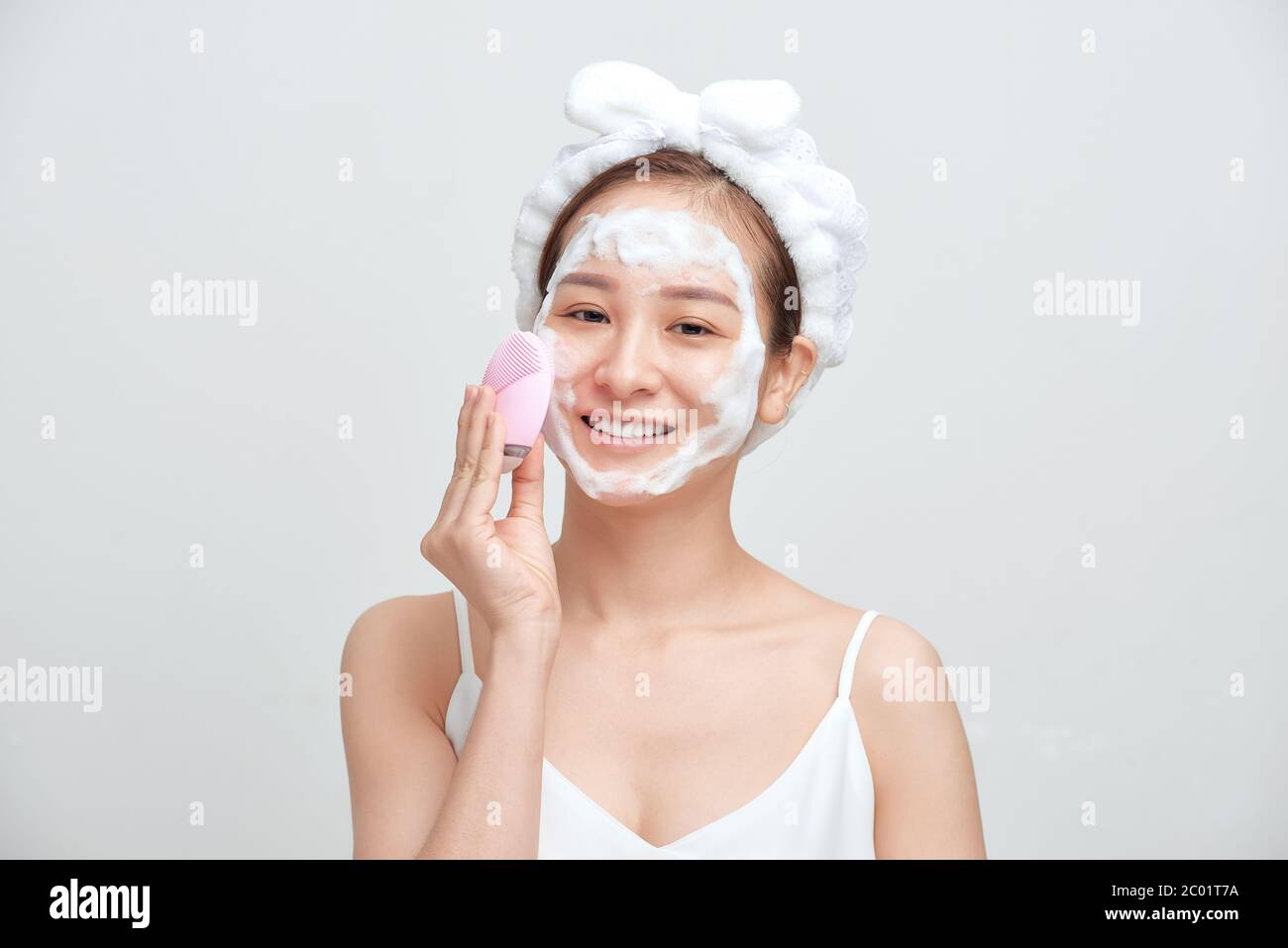 Happy young Asian woman applying foaming cleanser on her face and ...