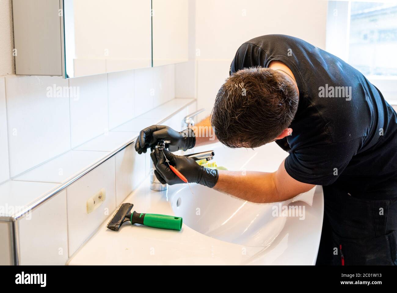 A man cleaning a bathroom sink with a scraper blade and micro fiber ...