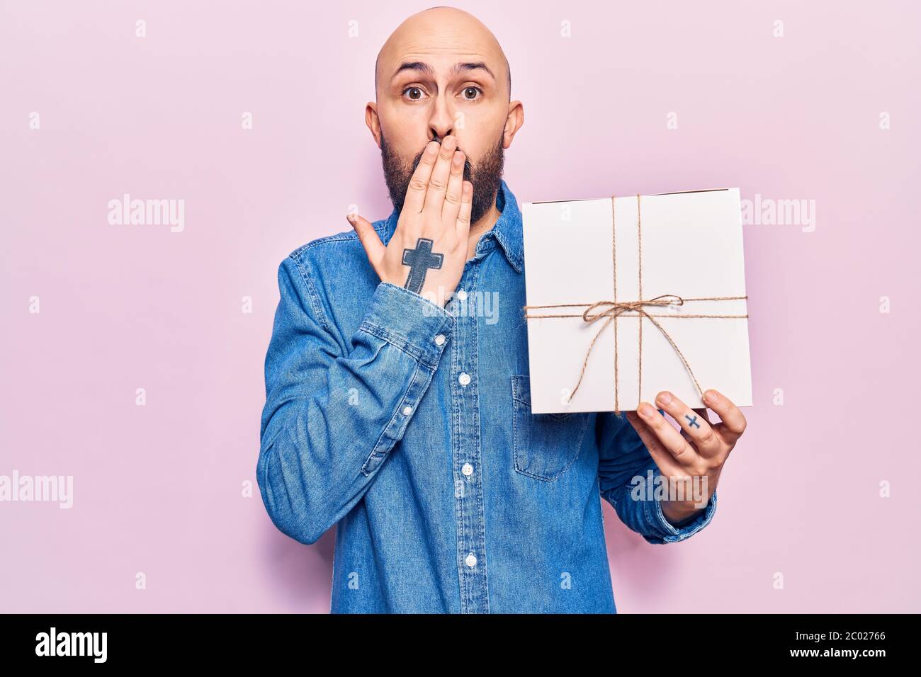 Young handsome man holding gift covering mouth with hand, shocked and ...