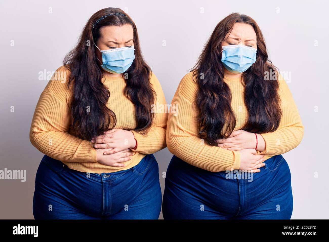 Young plus size twins wearing medical mask with hand on stomach because ...
