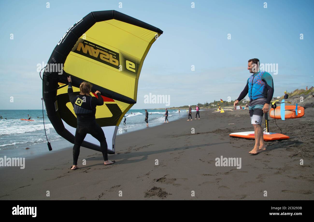 A man stands on a beach practicing with a hand held wing for hydrofoil ...