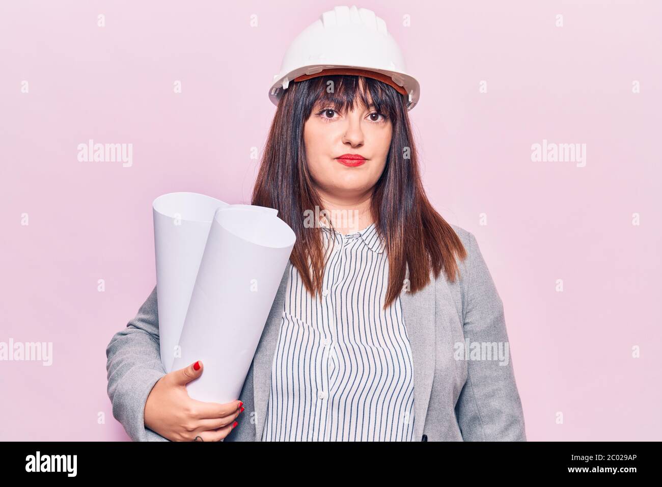 Young plus size woman holding paper blueprints thinking attitude and ...