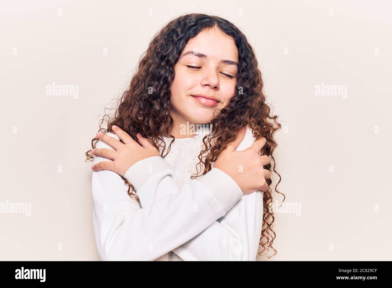 Beautiful kid girl with curly hair wearing casual clothes hugging ...