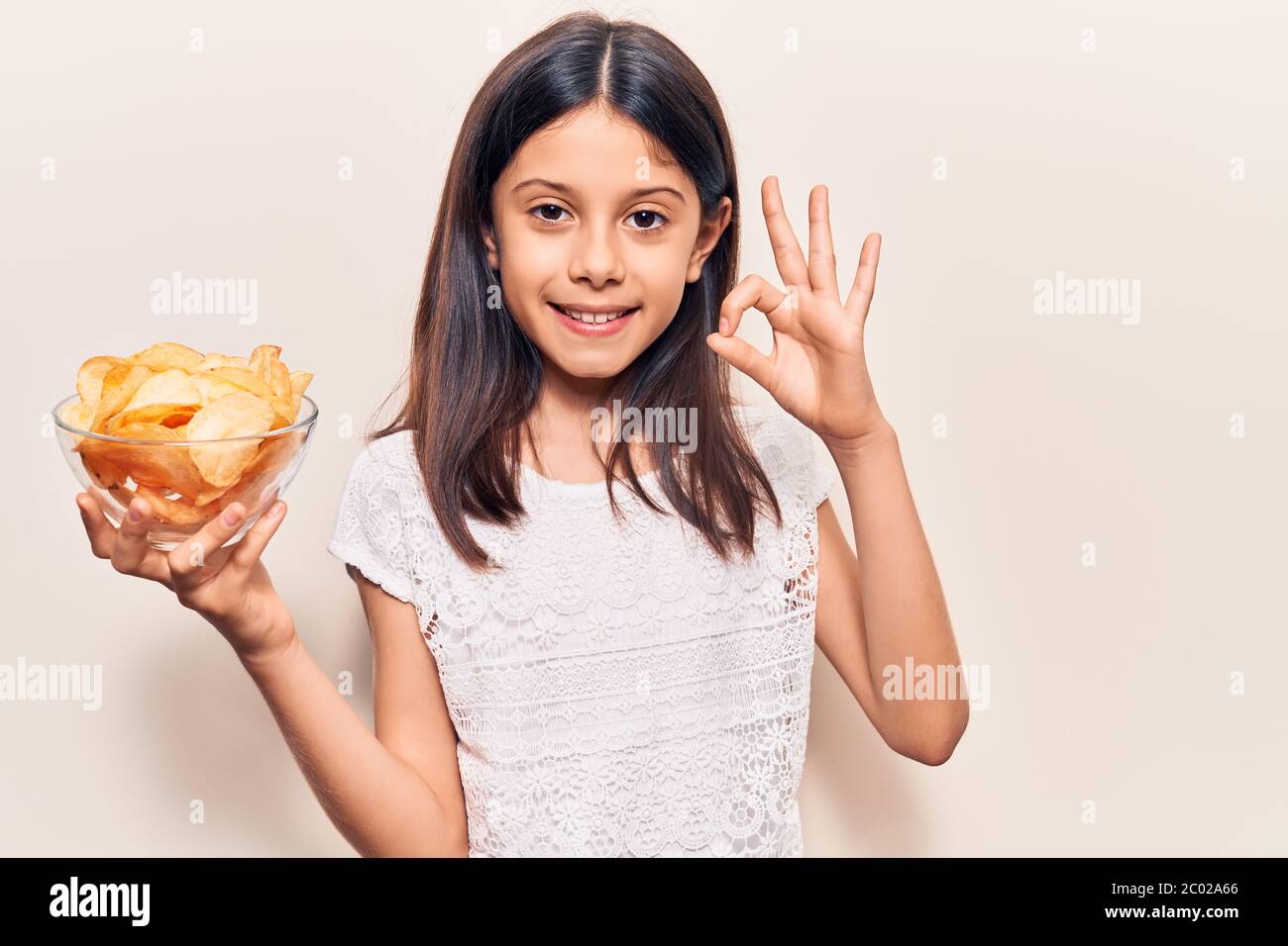 Beautiful child girl holding potato chip doing ok sign with fingers ...