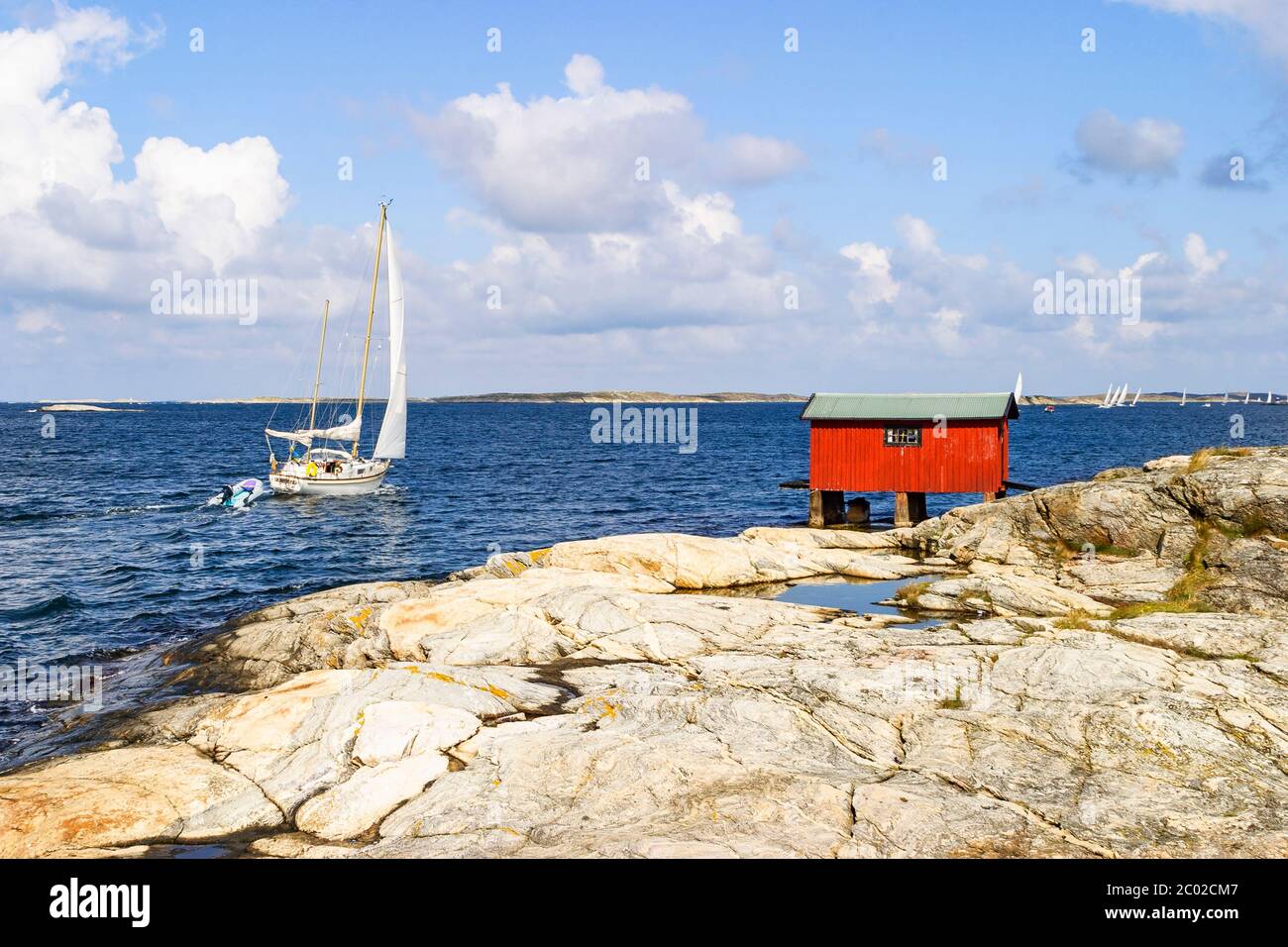 Red boathouse on a rock by the sea and a sailboat Stock Photo - Alamy