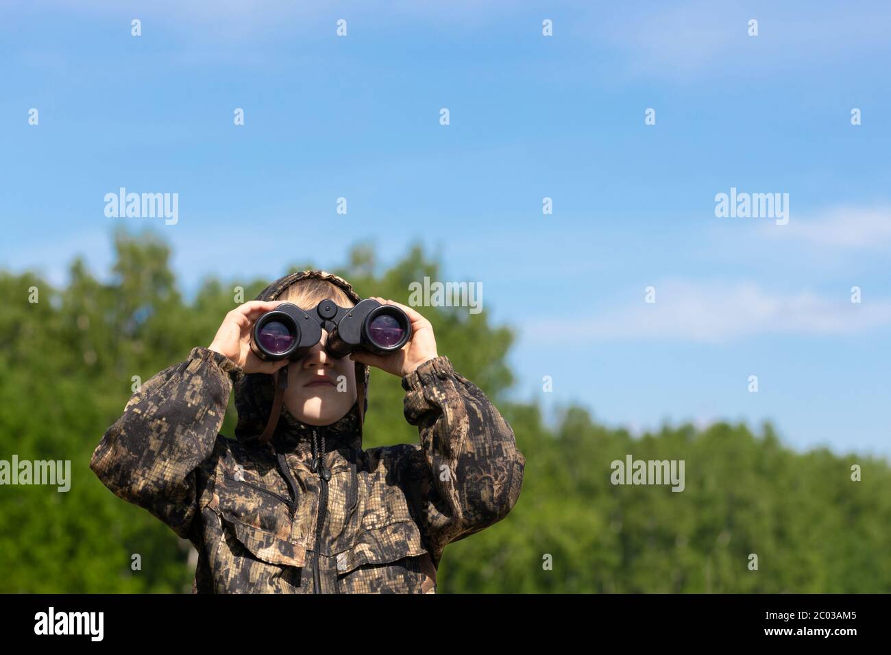 Scout boy looks through binoculars on camping trip in green forest ...