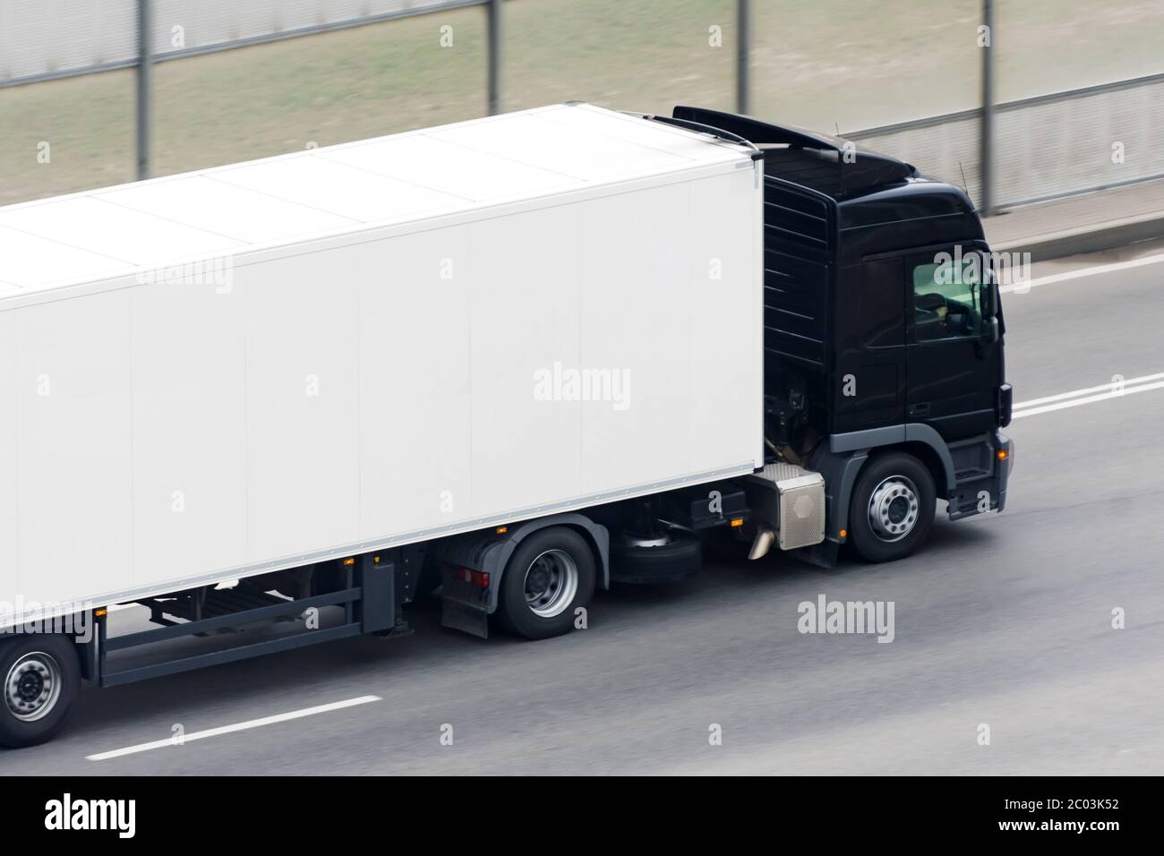 Truck with a black cab and a white trailer compartment drives on the ...