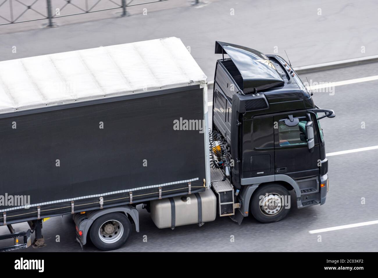 Truck with a black cab and a black trailer compartment drives on the ...