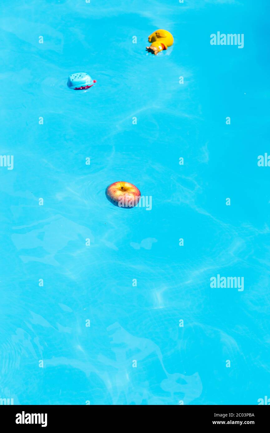 Vertical photo of one apple and toys floating in the water of a pool ...