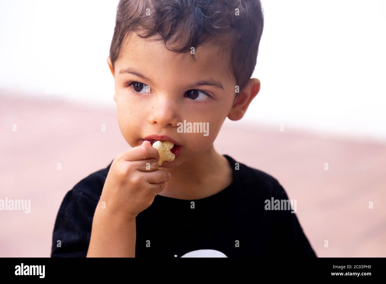 portrait of a child eating a potato chip with an absent expression ...