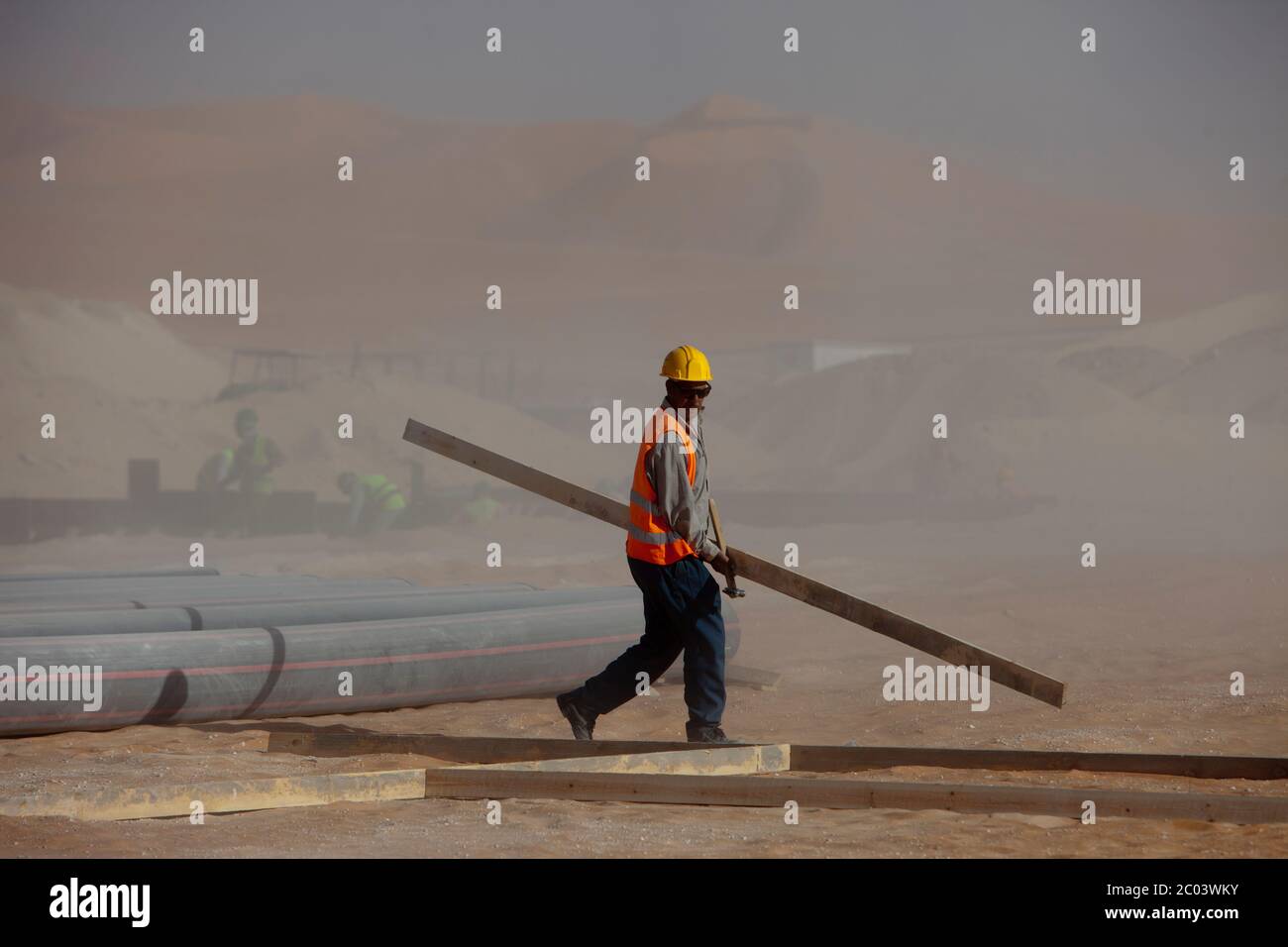 As a desert wind whips up dusty, a carpenter shifts timber to make a ...