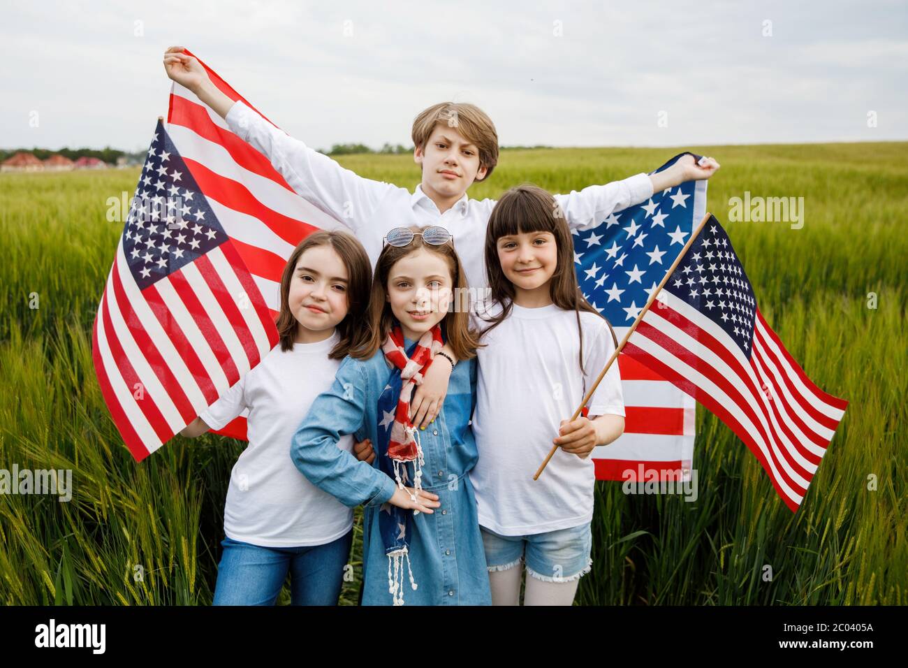 Four cheerful children stand in a field with an American flag in their ...