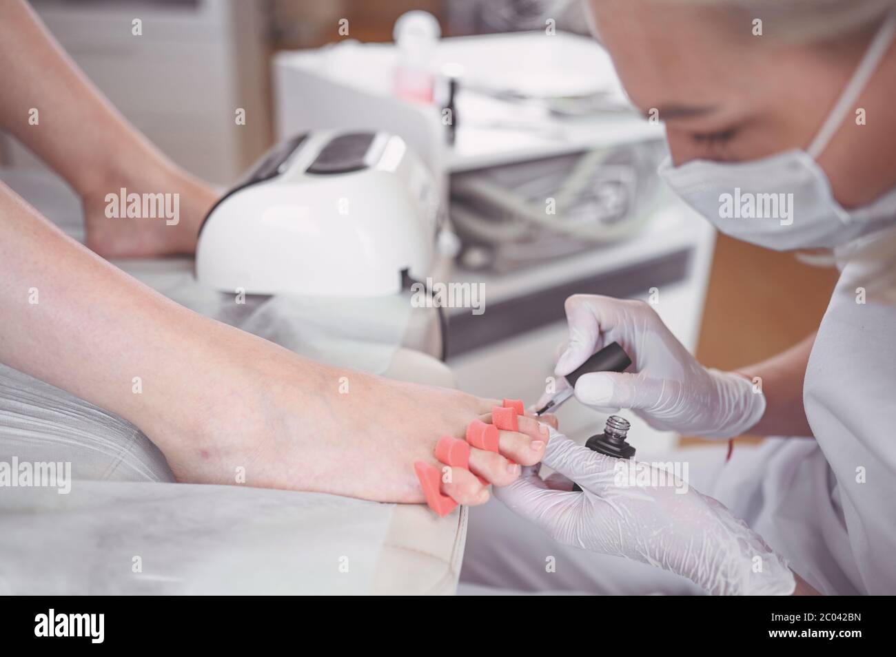 Pedicurist doing white nail polish on client legs using shellac lamp ...