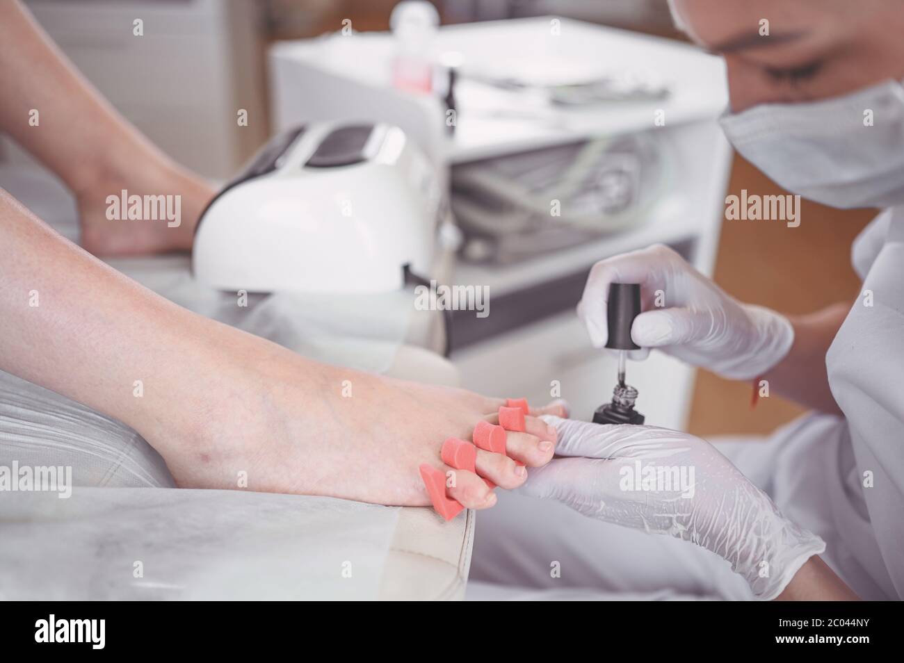 Pedicurist doing white nail polish on client legs using shellac lamp ...