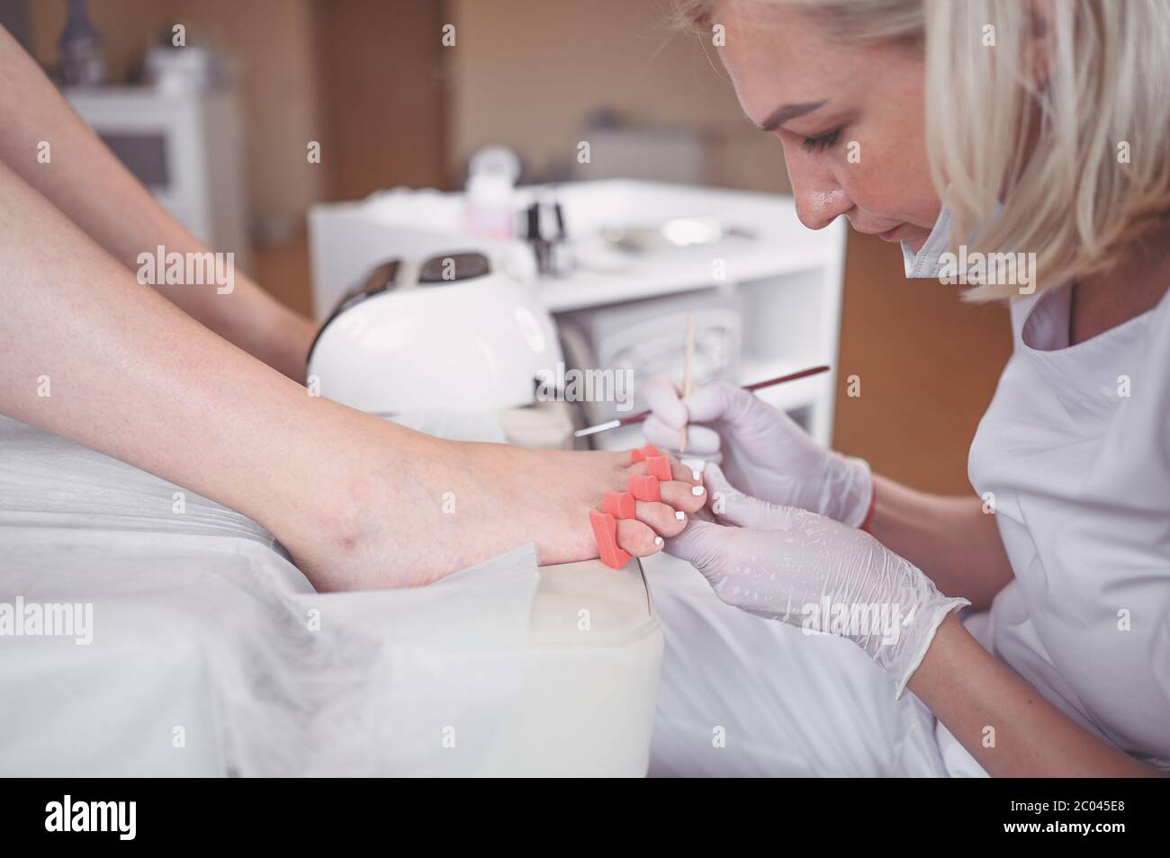 Pedicurist doing white nail polish on client legs using shellac lamp ...