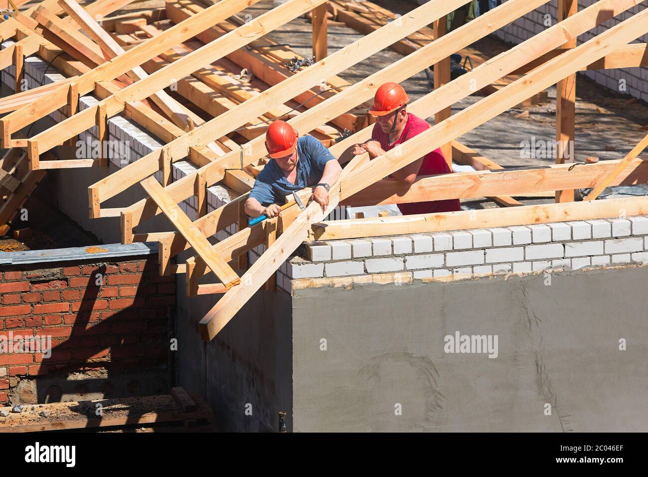 Two workers roofers in helmets surrounded by rafters and beams at ...