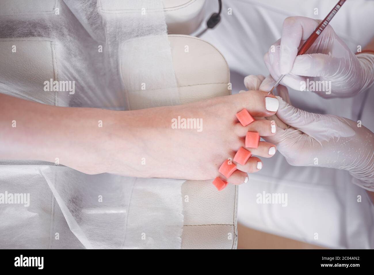 Pedicurist doing white nail polish on client legs using shellac lamp ...