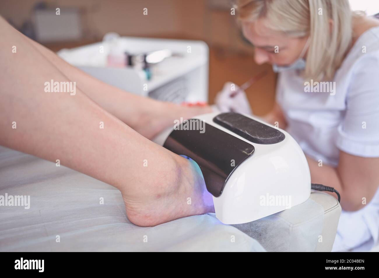 Pedicurist doing white nail polish on client legs using shellac lamp ...