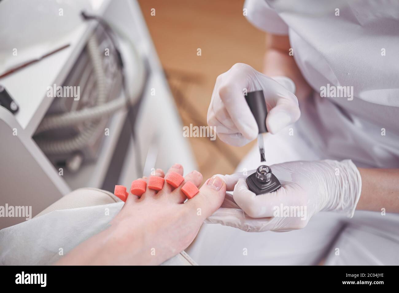 Pedicurist doing white nail polish on client legs using toe finger ...