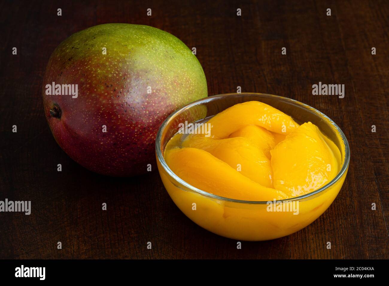 Canned mango slices in syrup in a glass bowl next to a whole fresh ...