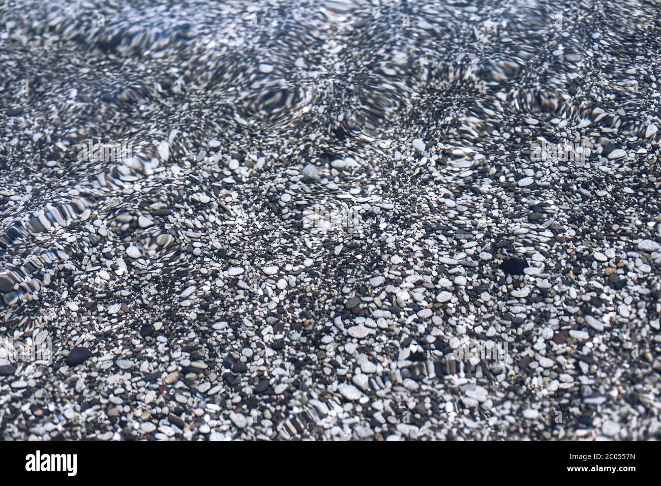 transparent clear calm water surface with small grey pebbles sea bottom ...