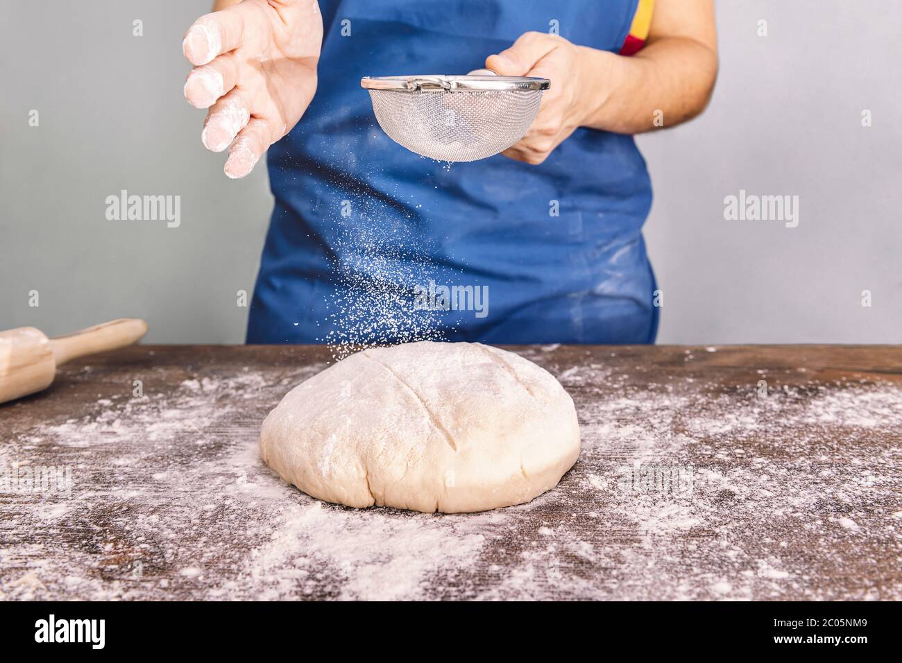 unrecognizable person putting flour on a rustic bread dough on a wooden ...