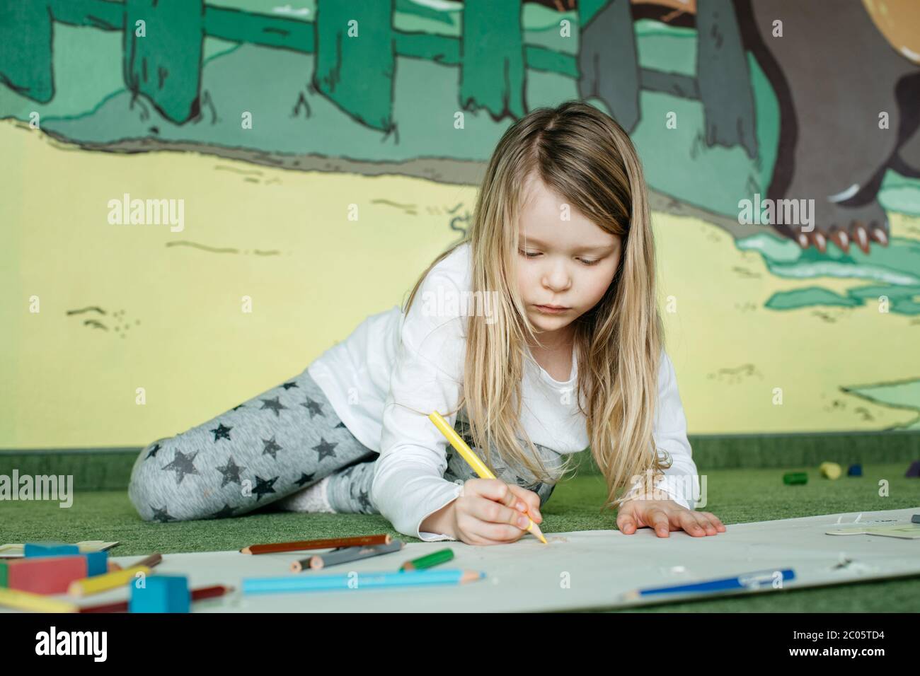 Girl lying on the floor and drawing a picture with colored pencils ...