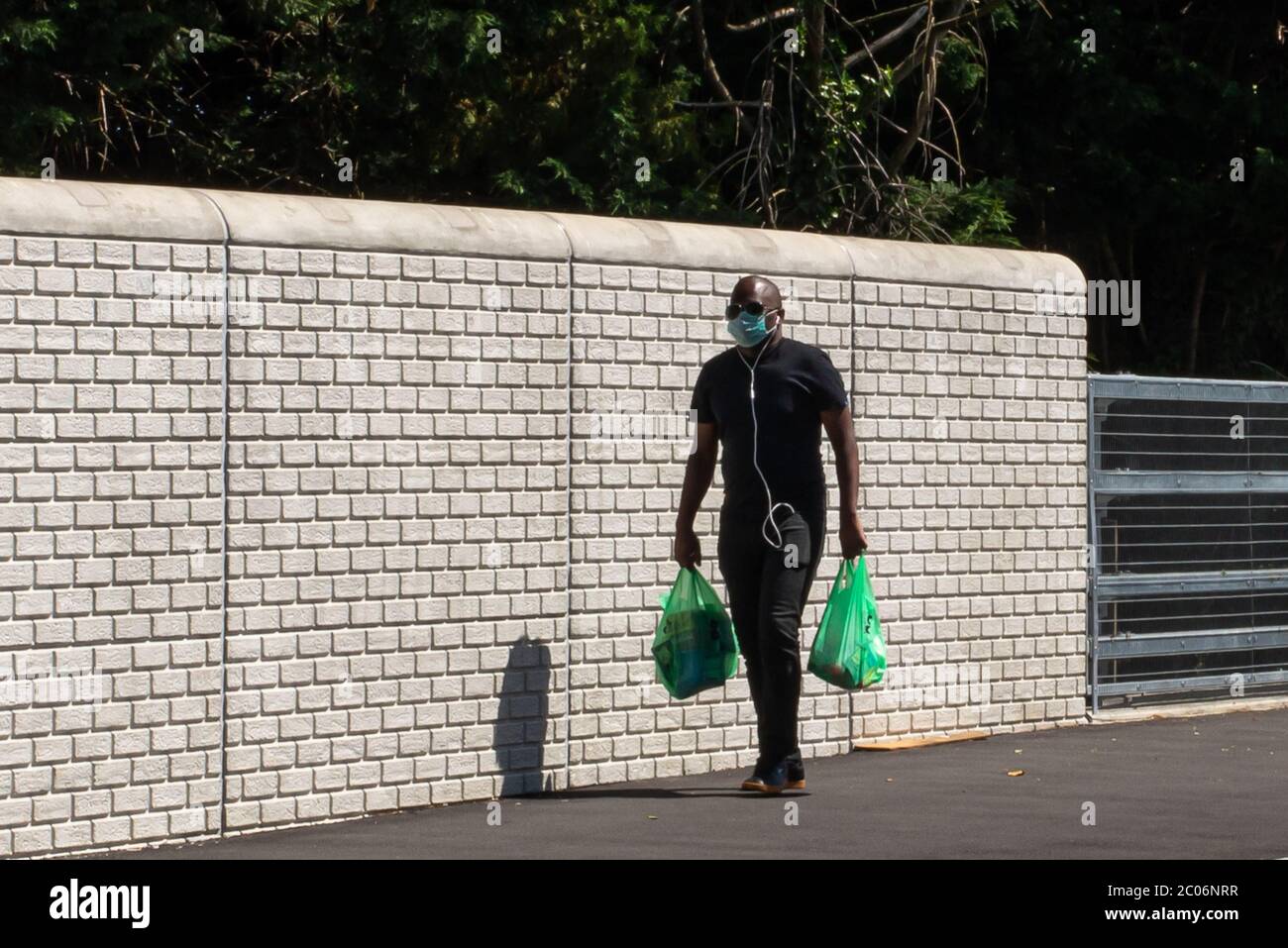 A lone man in black wearing a face mask carries his shopping home ...