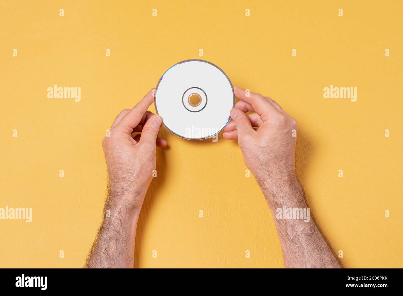 Male hands holding a CD-DVD in front of yellow background, editable ...