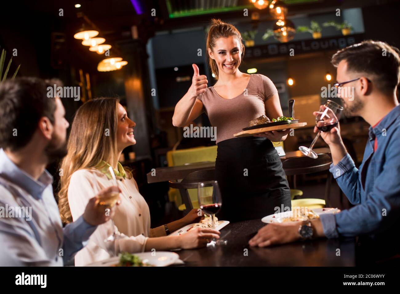 Pretty waiter woman serving group of friends with food in the restaura ...