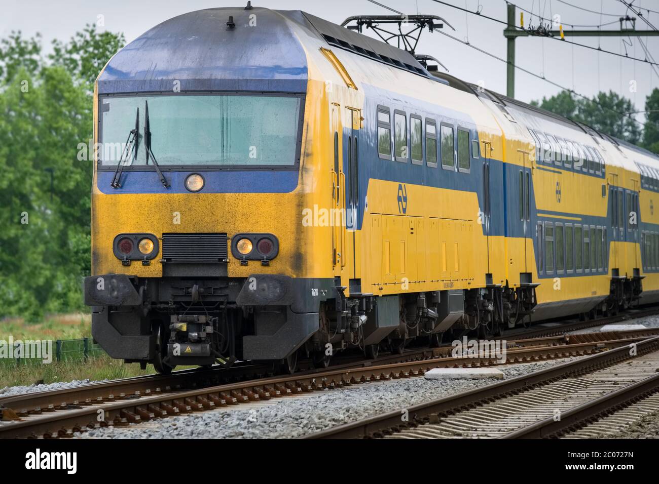 A somewhat dirty Dutch typical yellow-blue train runs on the rails near ...