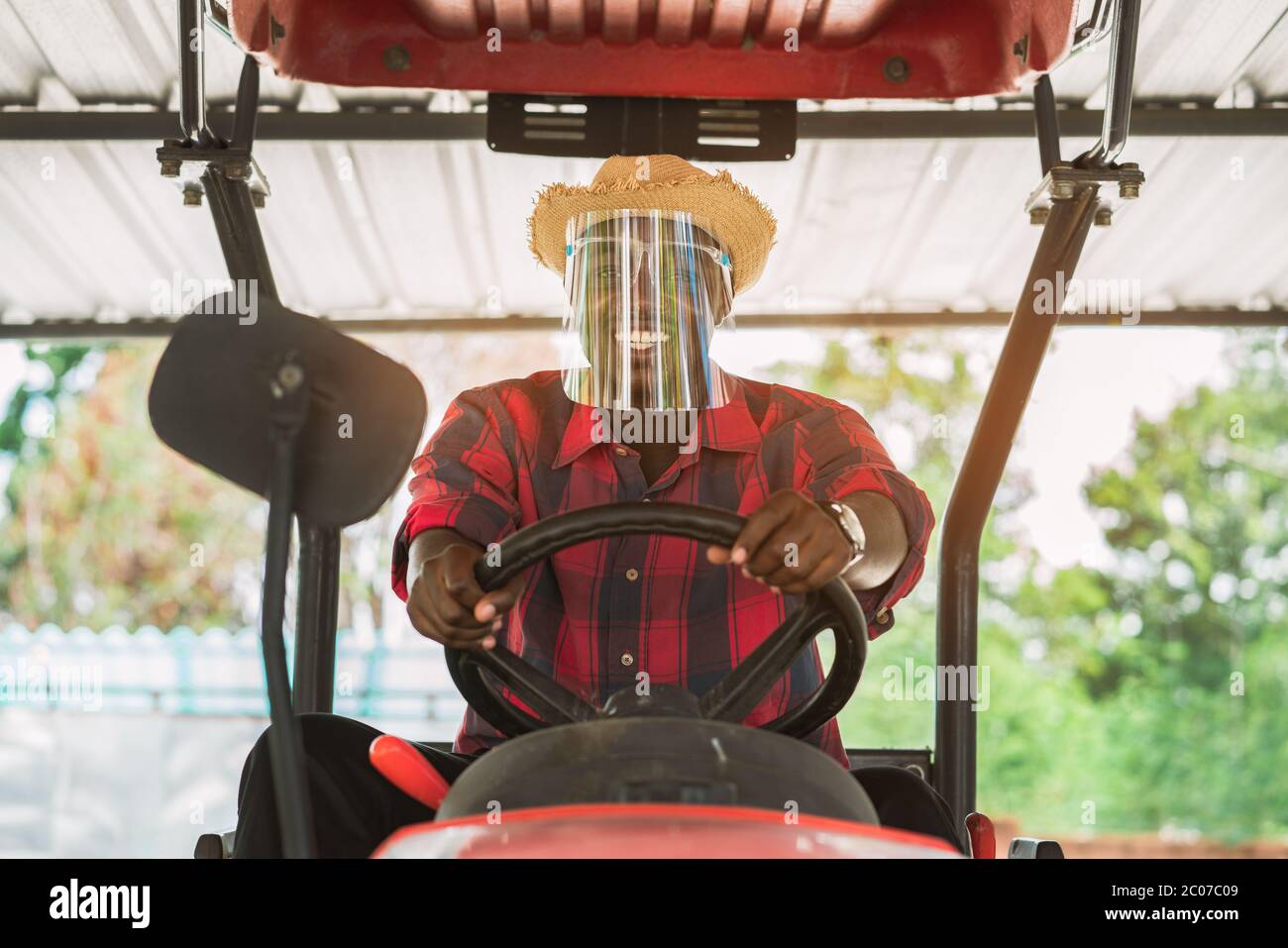 African farmer wear face shield and driving tractor in farm during ...