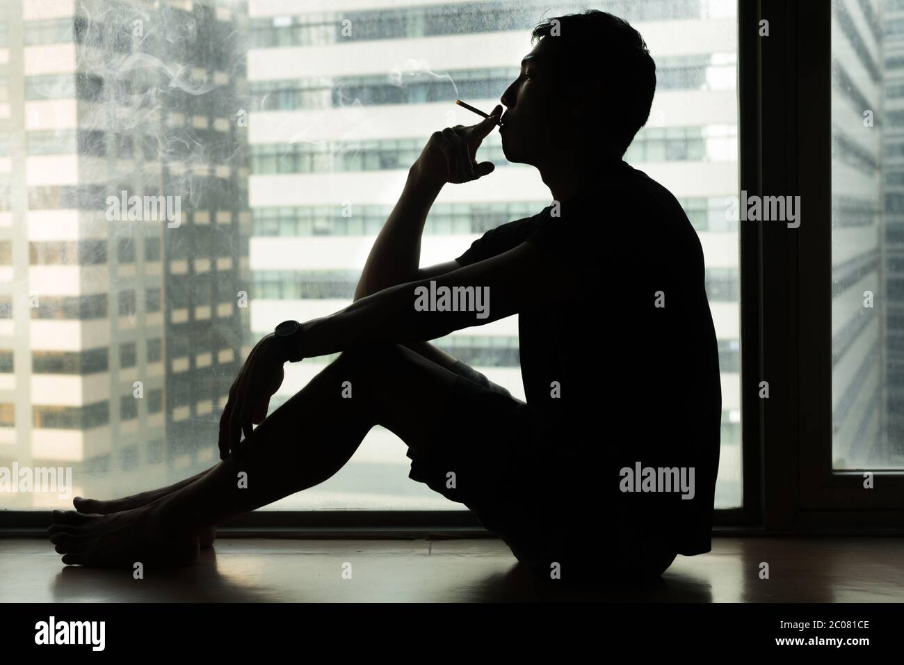 Sihoutte of a man smoking a cig in front of a window with a cityview ...