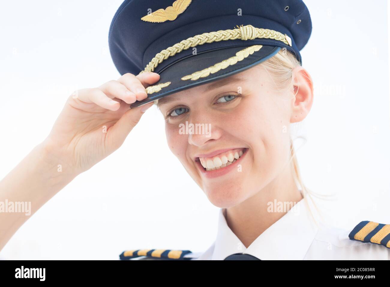 A happy female aviator pilot saluting with her hat at the airport ...
