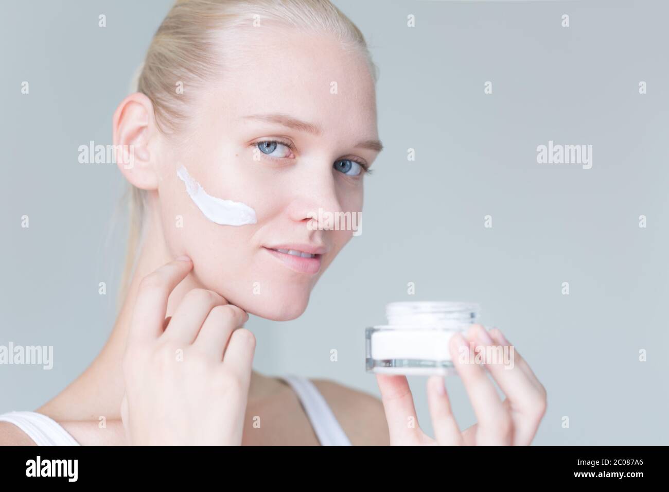 Female model moisturizing her face holding a cream jar in front of a ...