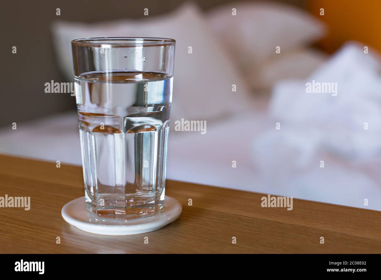 A glass of water sitting on a table next to a white bed in the morning ...