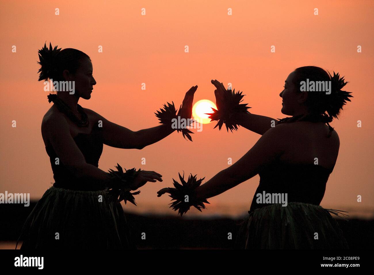 Traditional hula dancers (model released) appear to hold sun at sunset ...