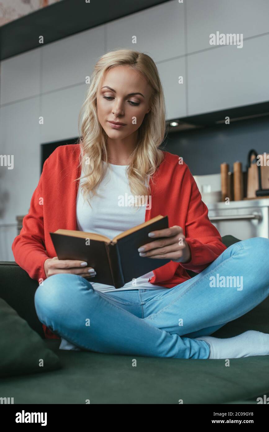 Attentive Young Woman Sitting On Sofa With Crossed Legs And Reading