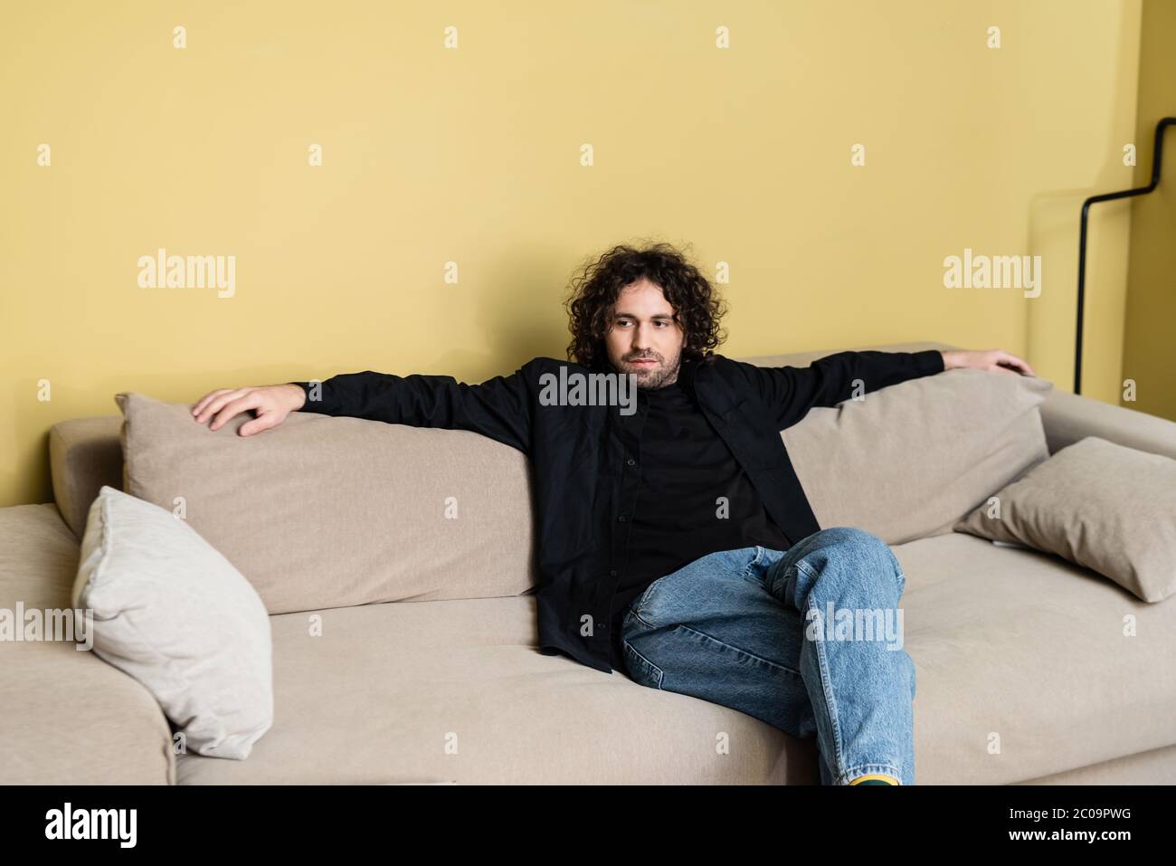 Handsome man sitting on couch in living room Stock Photo - Alamy