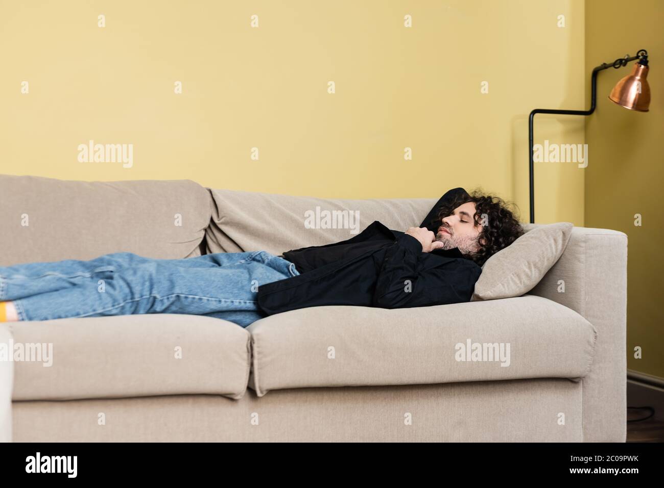 Side view of man lying on couch in living room Stock Photo - Alamy