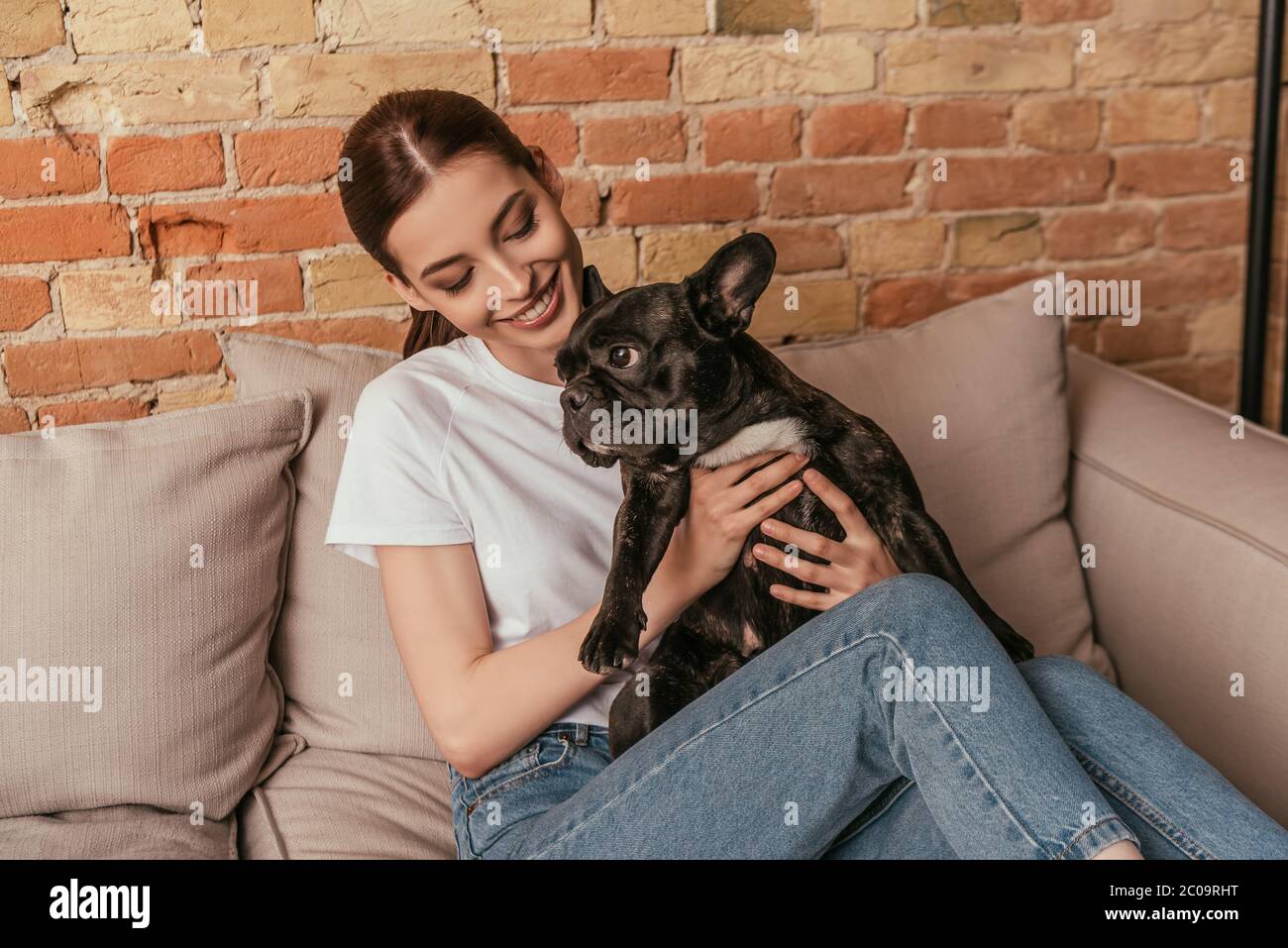 happy girl holding in arms cute french bulldog while sitting on sofa ...