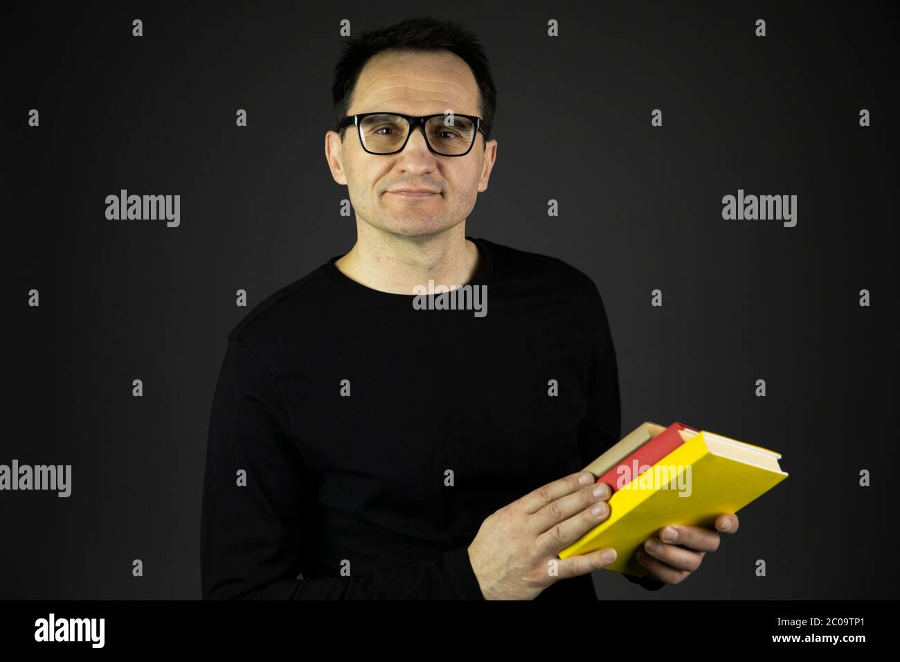 Pensive academic professor holding books in hands and looks at camera ...