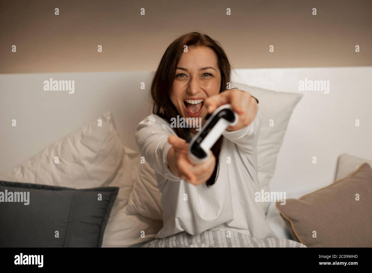 Young Caucasian girl in pajamas in bed plays video games on console ...