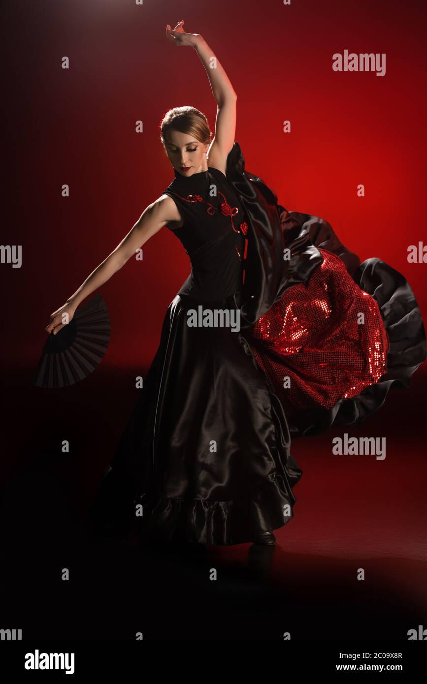 pretty flamenco dancer in dress holding fan while dancing on red Stock ...